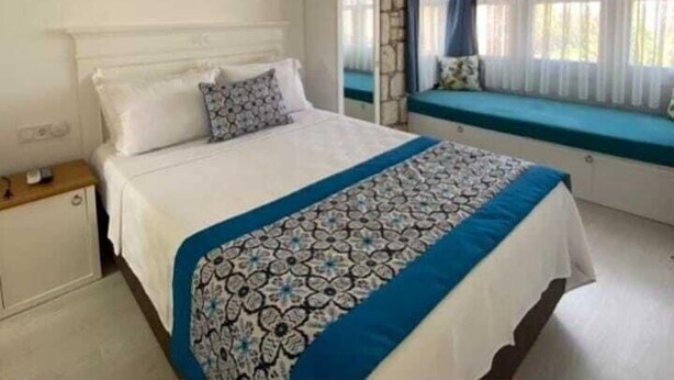 Quarto com cama, mesa de cabeceira, assento junto à janela e parede de pedra.