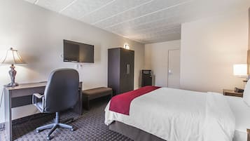 Quarto de hotel com cama, escrivaninha, cadeira, televisão, guarda-roupa e banheiro.