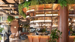 Uma área de bar moderna com diversas opções de assento, incluindo banquetas e mesas, e um display bem abastecido de vinhos e bebidas espirituosas.