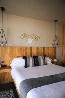 Cama bem arrumada com cabeceira de madeira, duas mesas de cabeceira e luminárias pendentes.