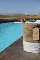 Uma cesta de palha com uma etiqueta que diz "POOL TOWELS" pela "TOALLAS DE ALBERCA", colocada à beira da piscina.