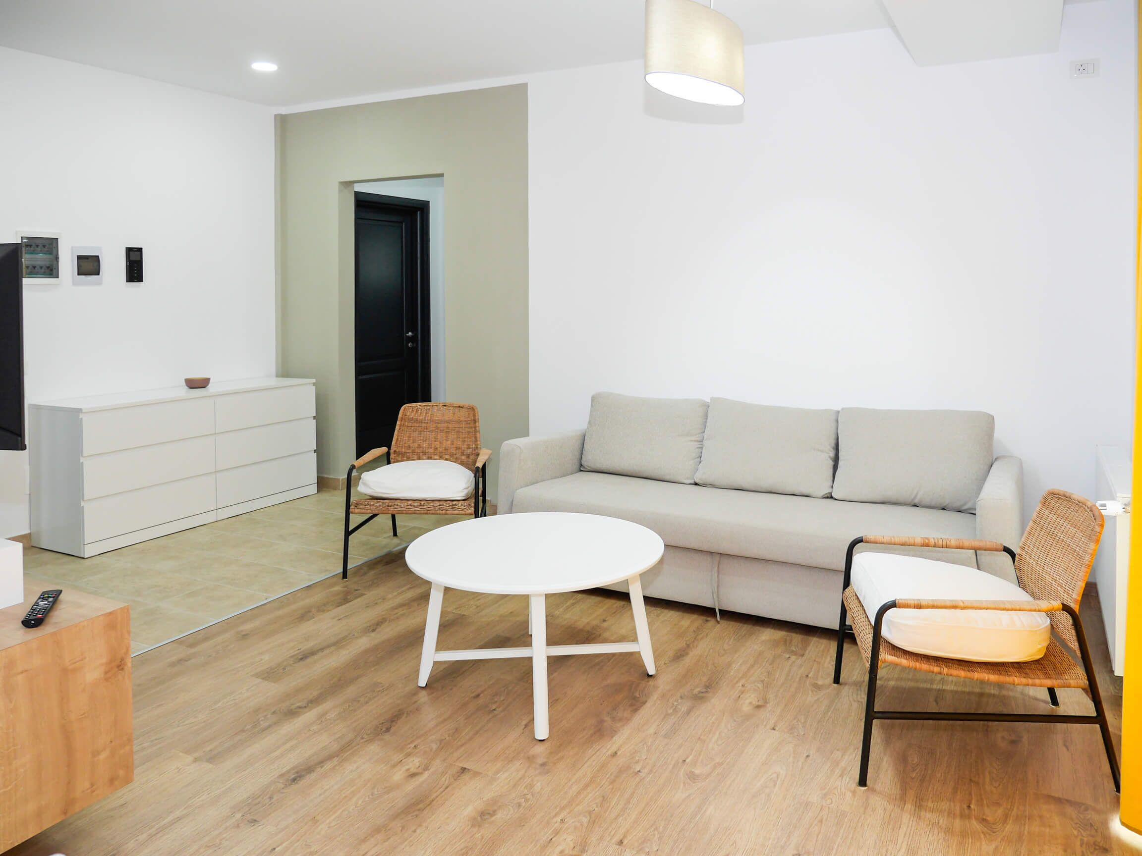 Uma sala de estar moderna com um sofá, duas cadeiras de vime, uma mesinha branca e um armário branco.