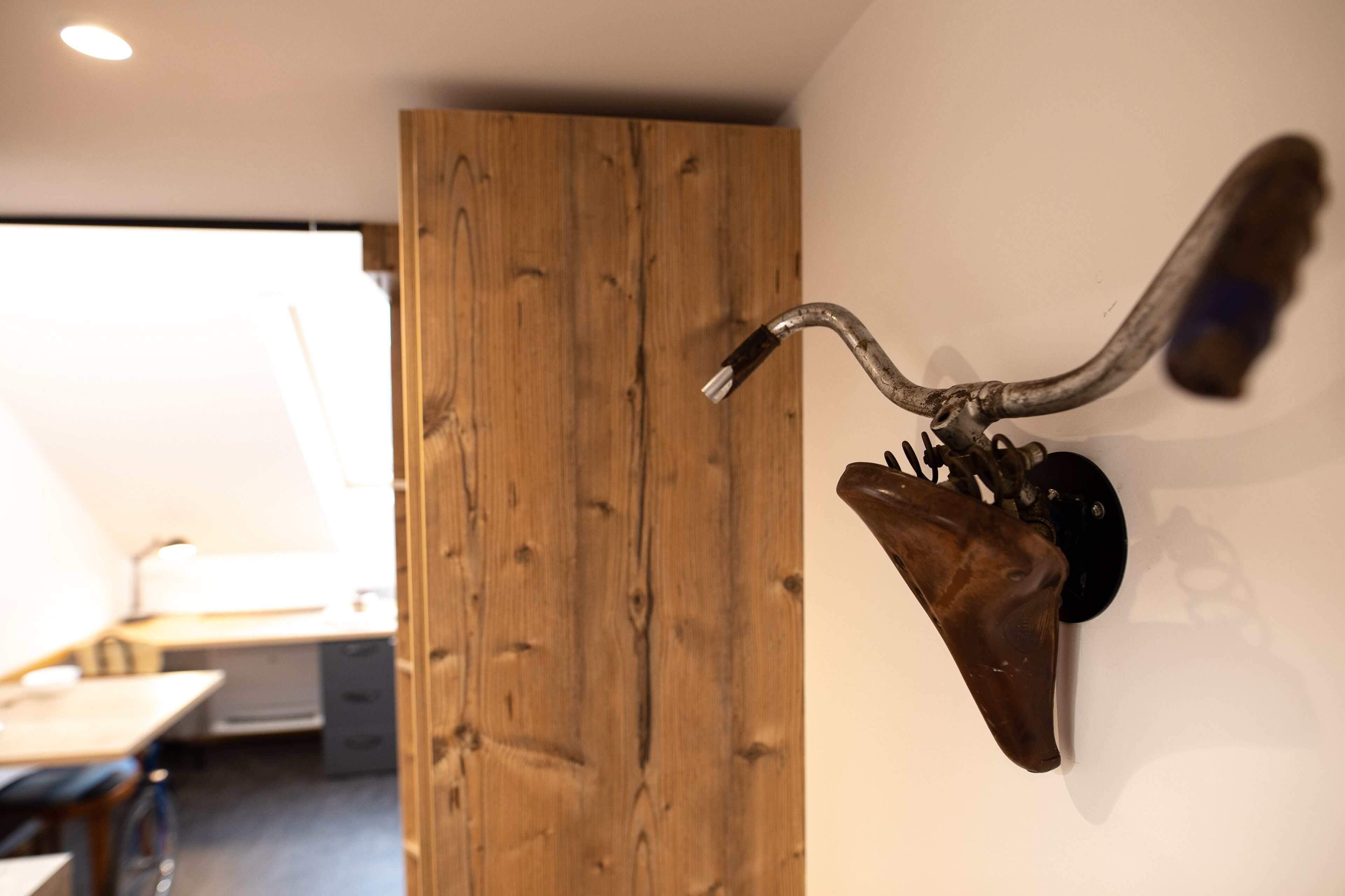 Quarto com porta de madeira, uma escultura na parede e vislumbre de uma sala de jantar com mesa e cadeiras.
