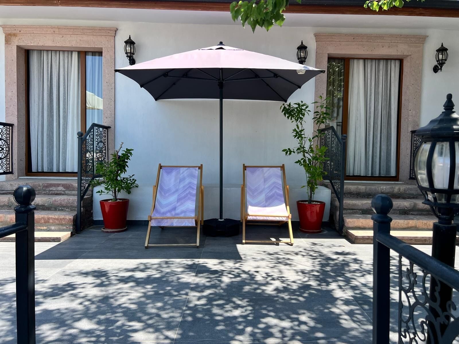 Dois cavaletes de madeira com suportes para tela, colocados sob um grande guarda-sol em um pátio calçado.