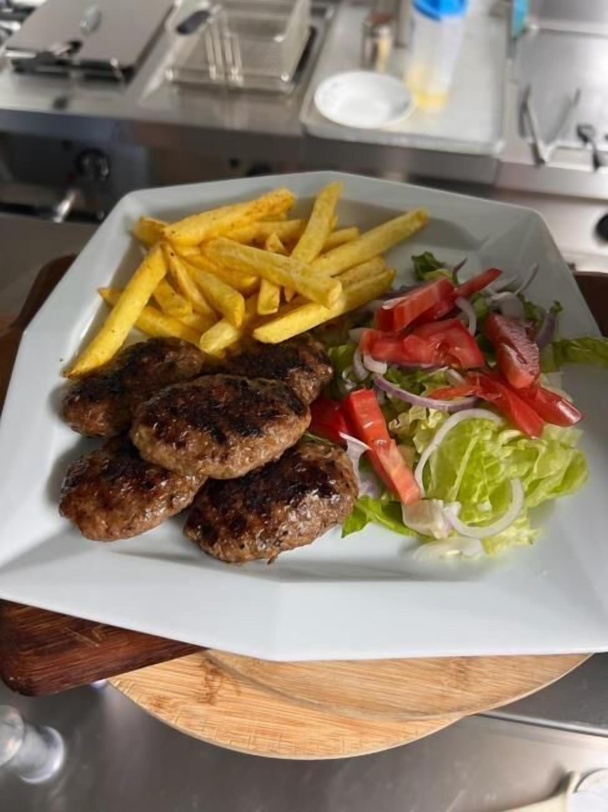 Um prato com três hambúrgueres grelhados, batatas fritas e uma salada verde mista com tomates e cebolas.