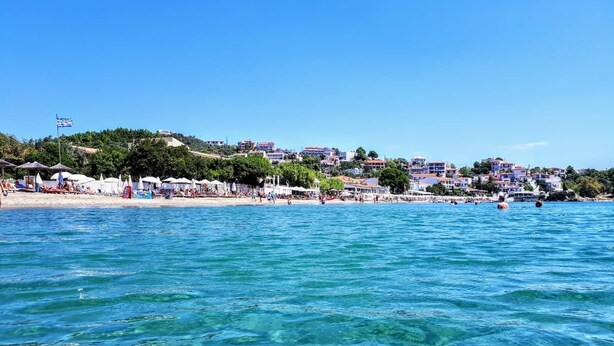 Uma cidade costeira com uma praia, águas azul-claras e edifícios numa encosta.