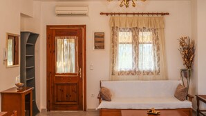 Uma sala de estar com porta de madeira, um sofá, uma mesa de centro e um ar condicionado fixado na parede.