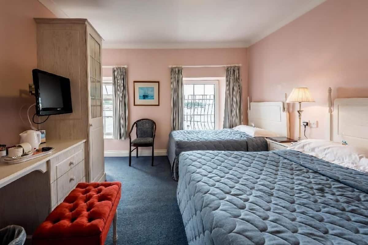 Quarto de hotel com duas camas, uma escrivaninha, uma cadeira, uma televisão e uma janela com cortinas.