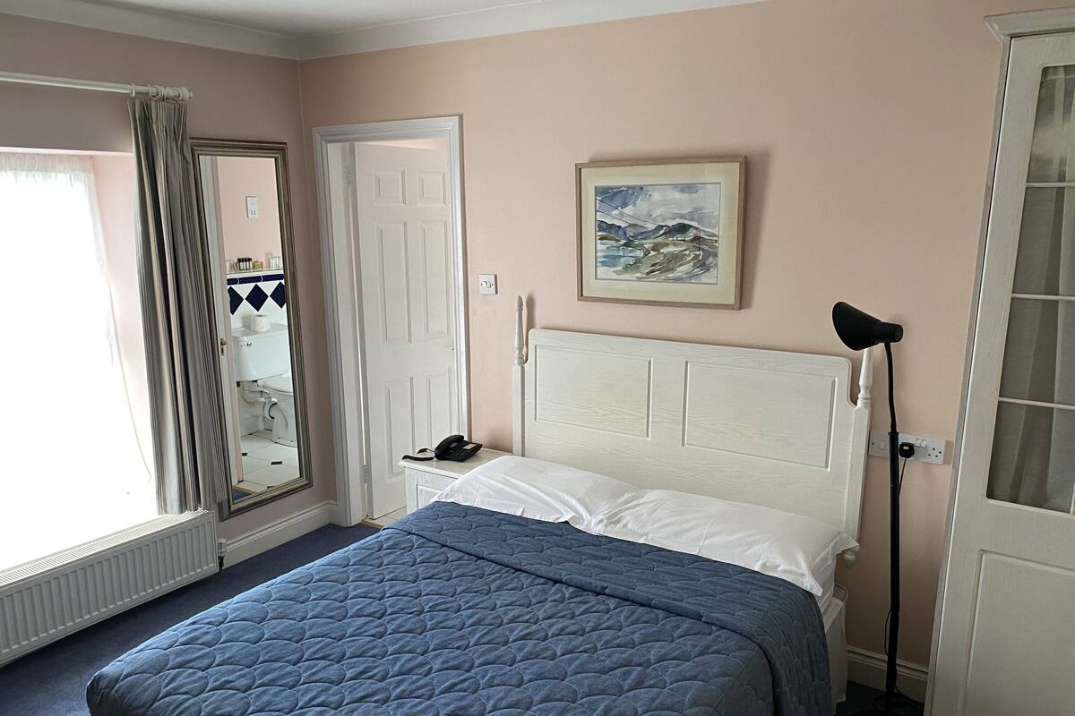 Quarto com cama, mesa de cabeceira, luminária, quadro na parede e porta.
