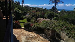 Um jardim com caminho de pedra, vegetação exuberante e vista para o oceano.