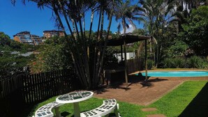 Um quintal com piscina, duas mesas brancas ao ar livre e uma pérgola.