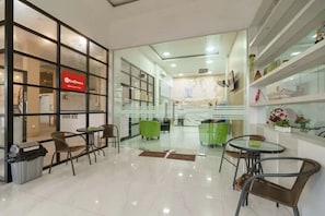 Um lobby de hotel moderno com divisórias de vidro, um letreiro RedDoorz e uma área de jantar com mesas e cadeiras.