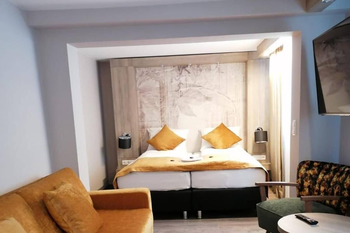 Quarto de hotel moderno com sofá, uma mesa pequena e uma cama com cabeceira.