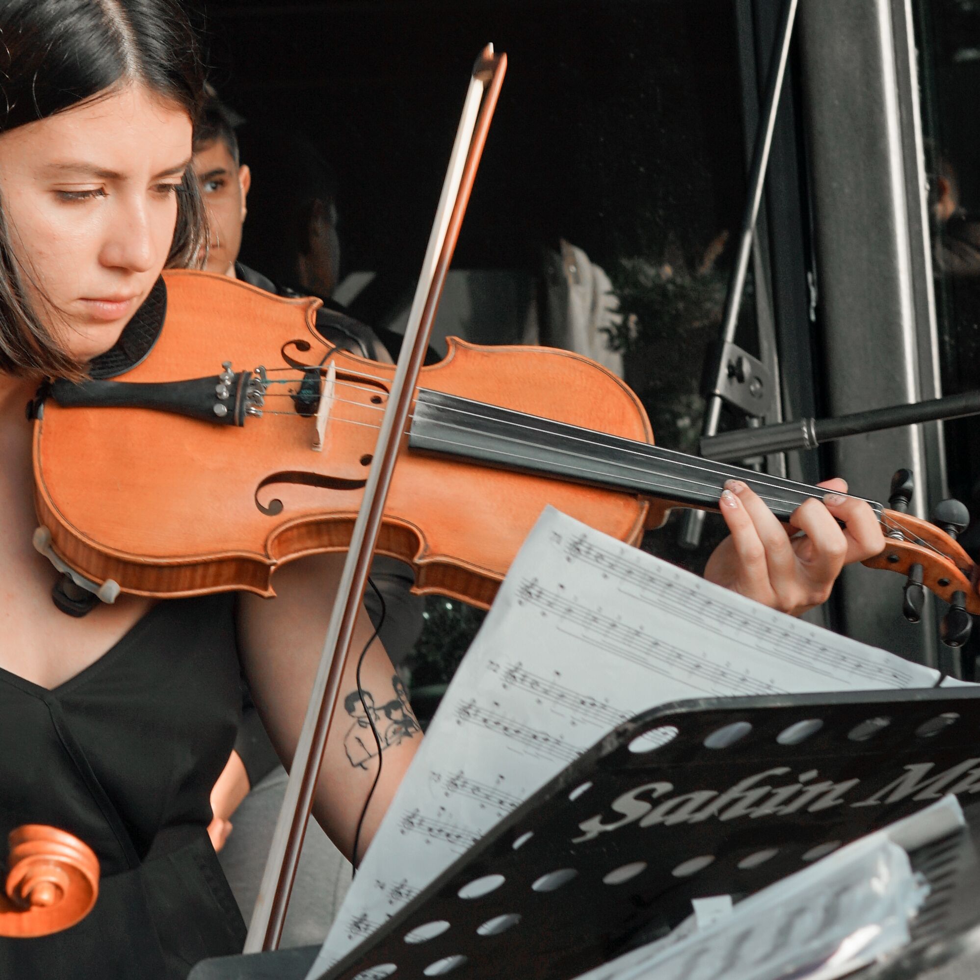 Uma pessoa tocando violino com partitura na mão.