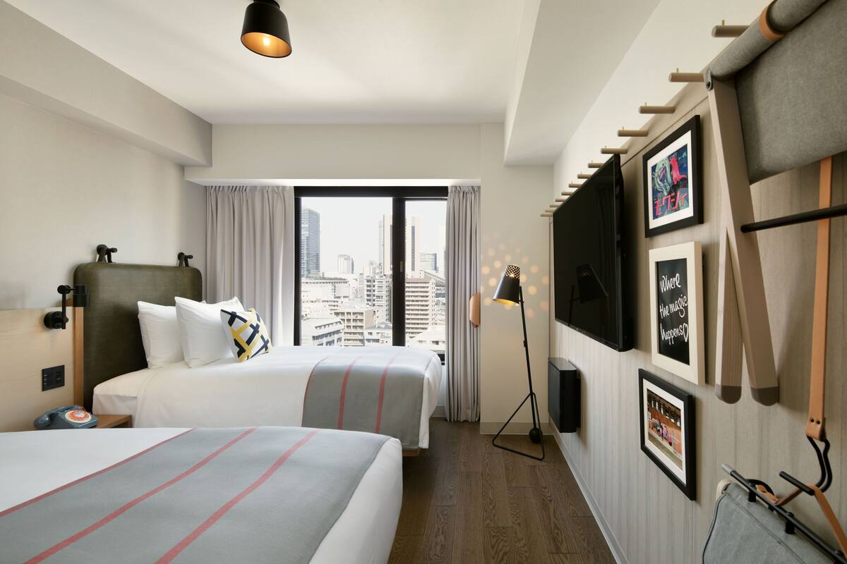 Quarto de hotel com duas camas, vista para a cidade, televisão de tela plana e televisão fixada na parede.