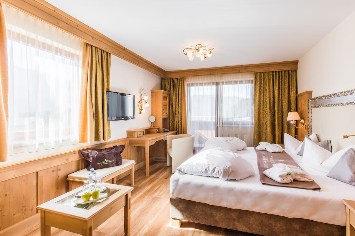Quarto de hotel com cama, escrivaninha, cadeira, televisão e janela com cortinas.