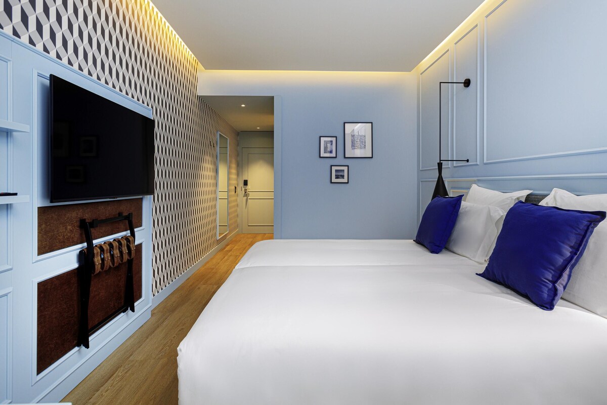Quarto de hotel moderno com uma cama grande, uma televisão na parede e piso de madeira.