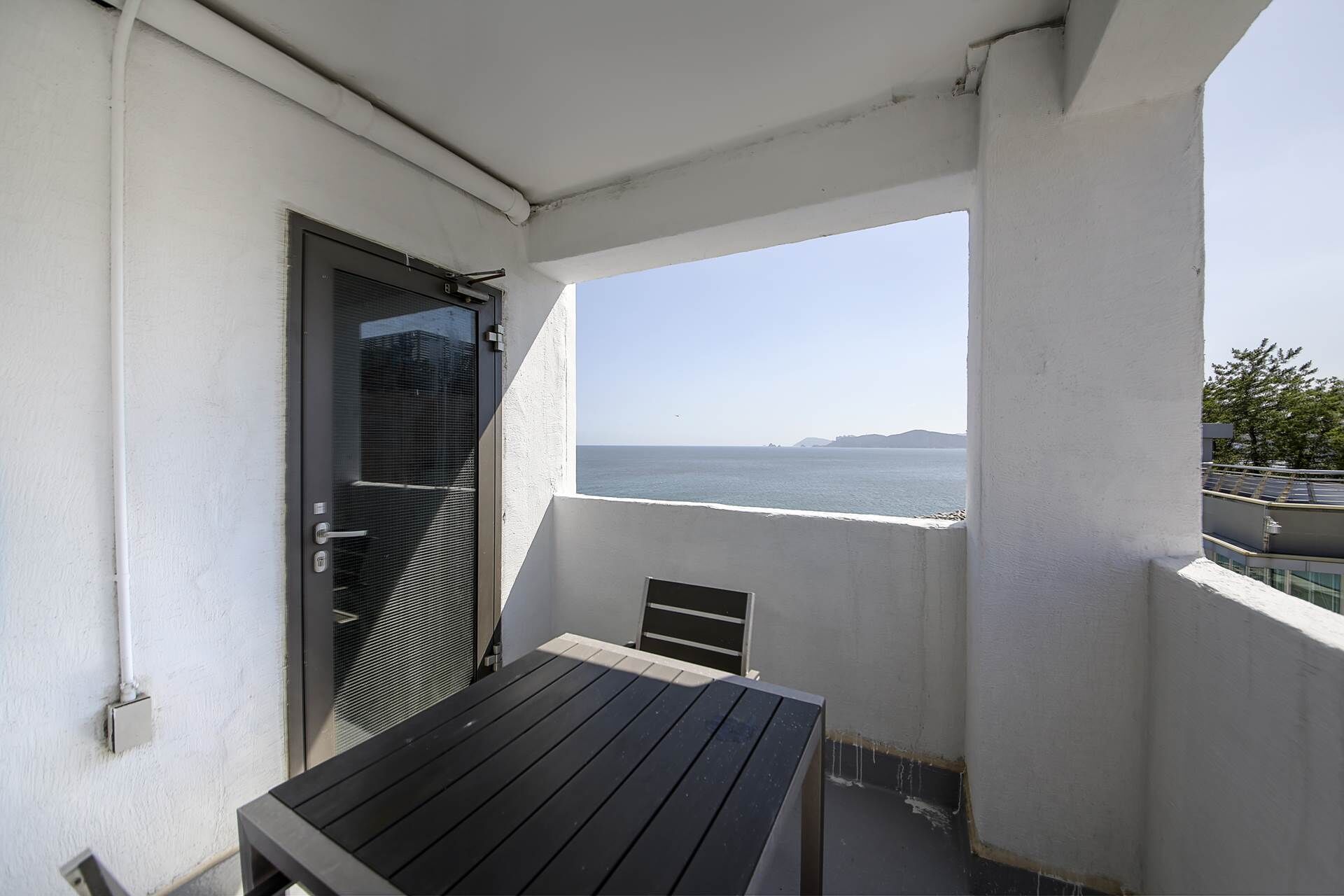 Uma varanda com mesa, cadeiras, uma porta e vista para o mar.