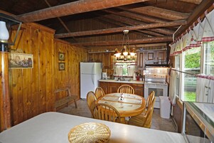 Um interior rústico de madeira com uma mesa de jantar, cadeiras, uma geladeira, um fogão e uma área de cozinha com armários de madeira e um lustre.