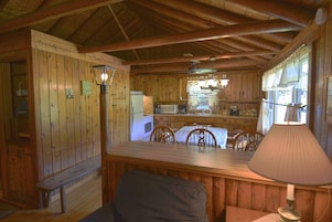 Interior de uma cabana de madeira com sala de jantar, cozinha e um banco.
