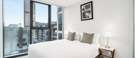 Quarto de hotel moderno com uma cama grande, um quadro na parede e vista para o horizonte urbano pela janela.