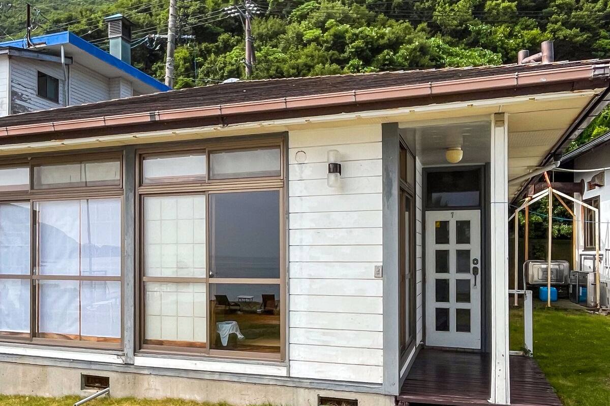 Uma casa térrea com varanda frontal, janelas amplas e uma porta.