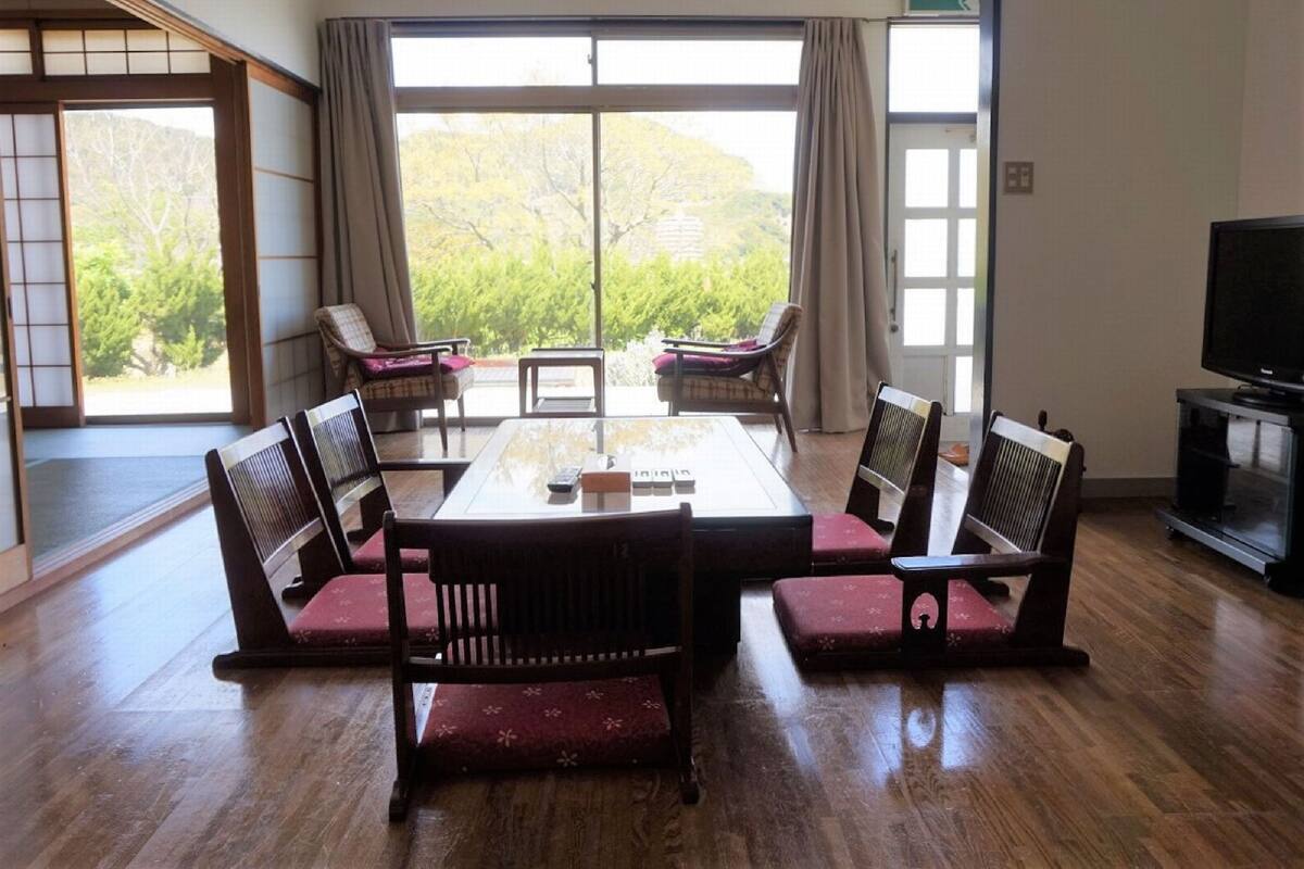Um quarto tradicional em estilo japonês, com tatames, uma mesa baixa com almofadas e uma televisão sobre um suporte.