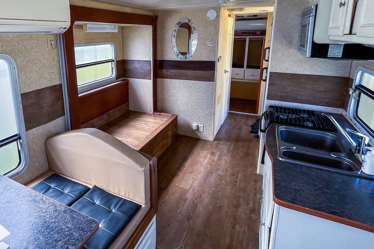 Interior compacto de uma RV, com cozinha compacta, área de estar com bancos acolchoados e uma pequena mesa.