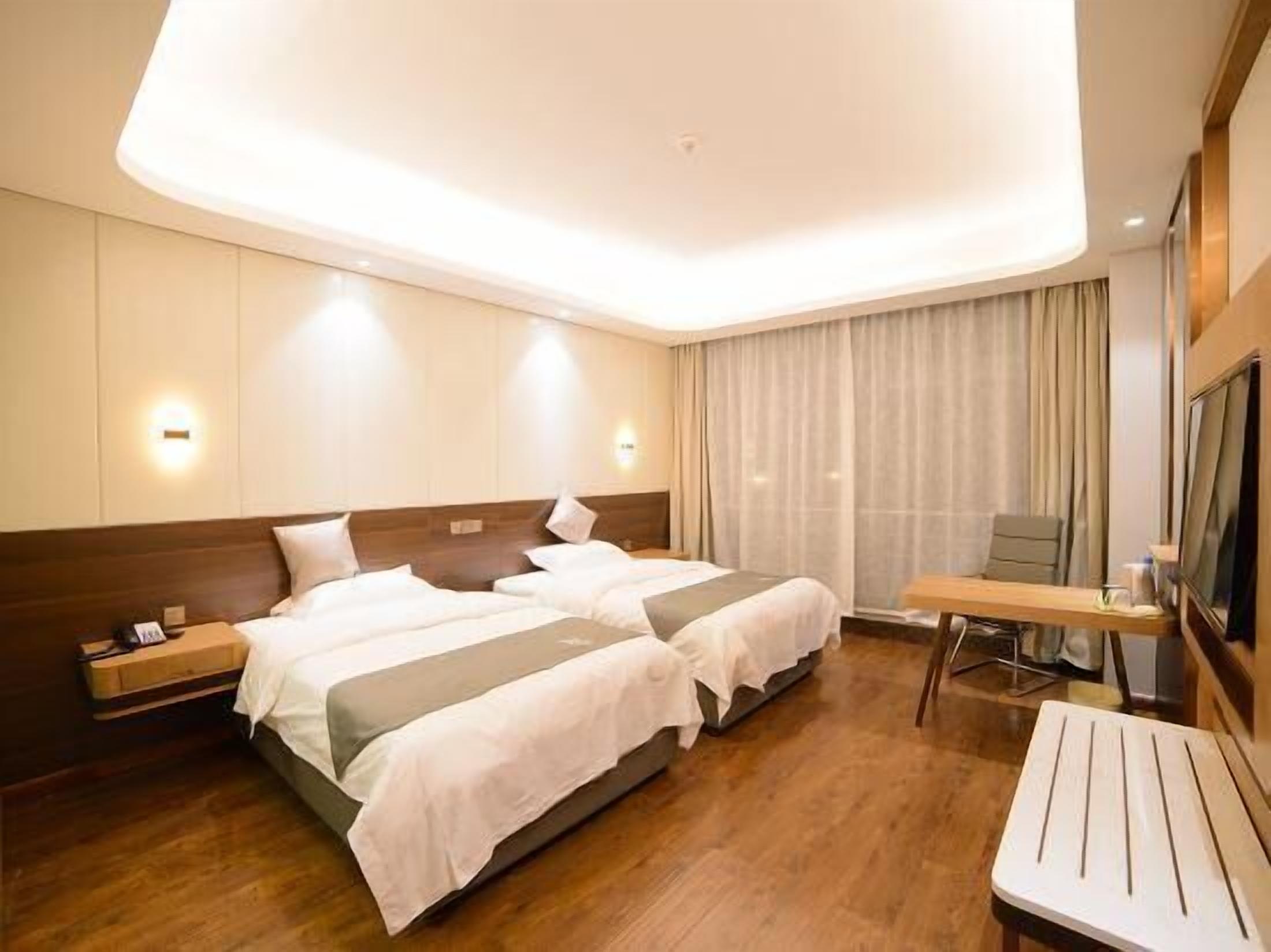 Quarto de hotel com duas camas, uma escrivaninha, uma cadeira e uma televisão.