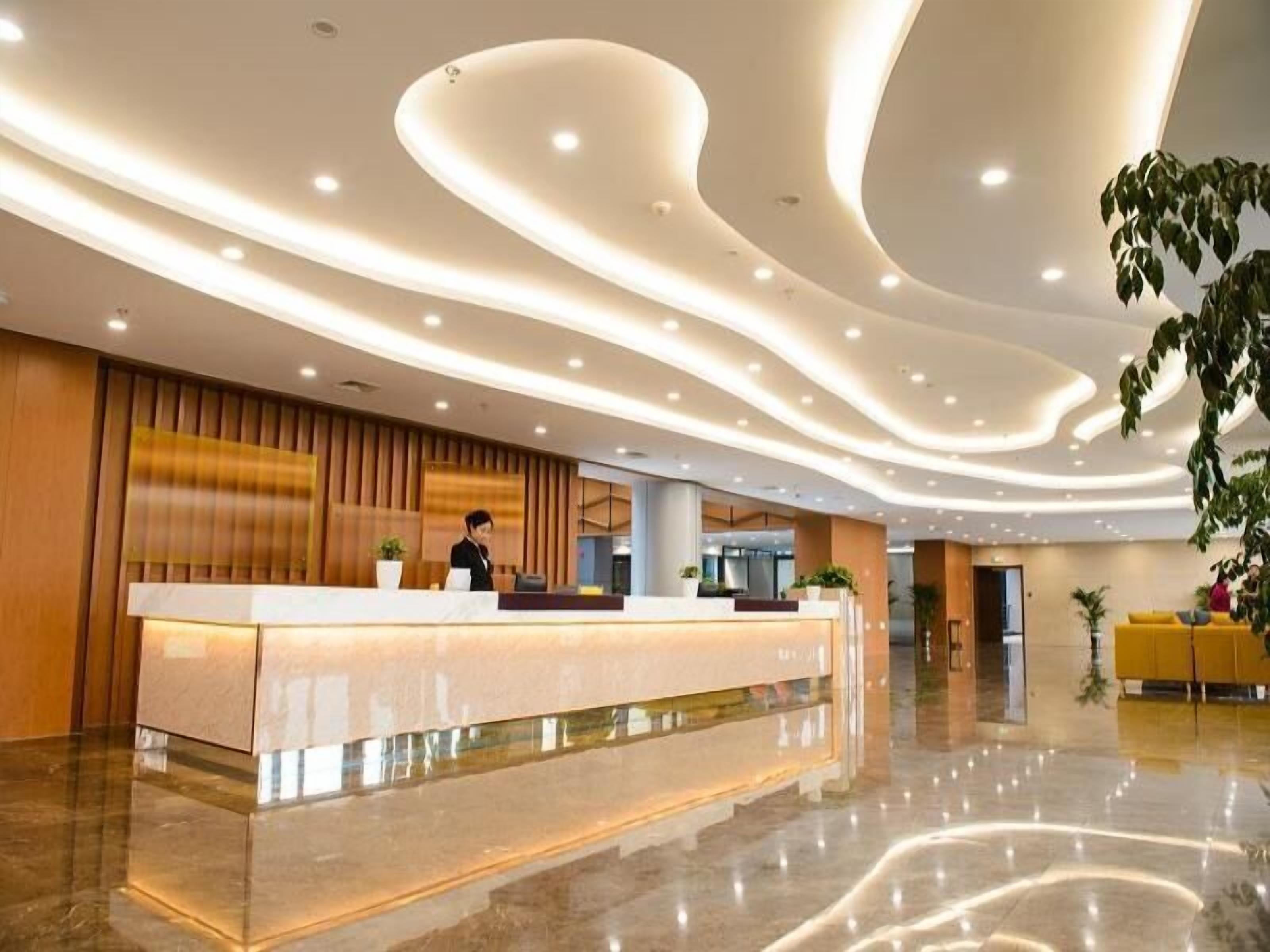 Um saguão de hotel moderno com balcão de recepção, painéis de madeira e uma planta grande.