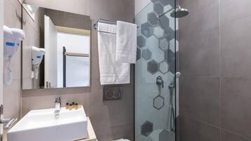 Casa de banho moderna com lavatório branco, espelho, secador de cabelo e chuveiro com azulejos hexagonais.