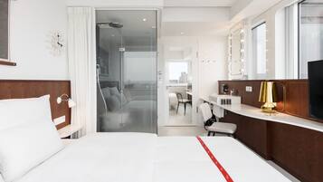 Quarto de hotel moderno com uma cama, uma escrivaninha, um espelho iluminado, uma televisão e vista para a cidade.