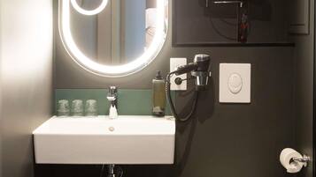 Casa de banho com lavatório branco, espelho com luz, secador de cabelo e um porta-toalhas.