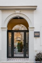 Entrada de um hotel com uma porta preta, uma placa com o nome "Palazzo 42" e piso de azulejos.