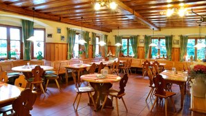 Um restaurante com mesas e cadeiras de madeira, cortinas verdes e piso de azulejos.