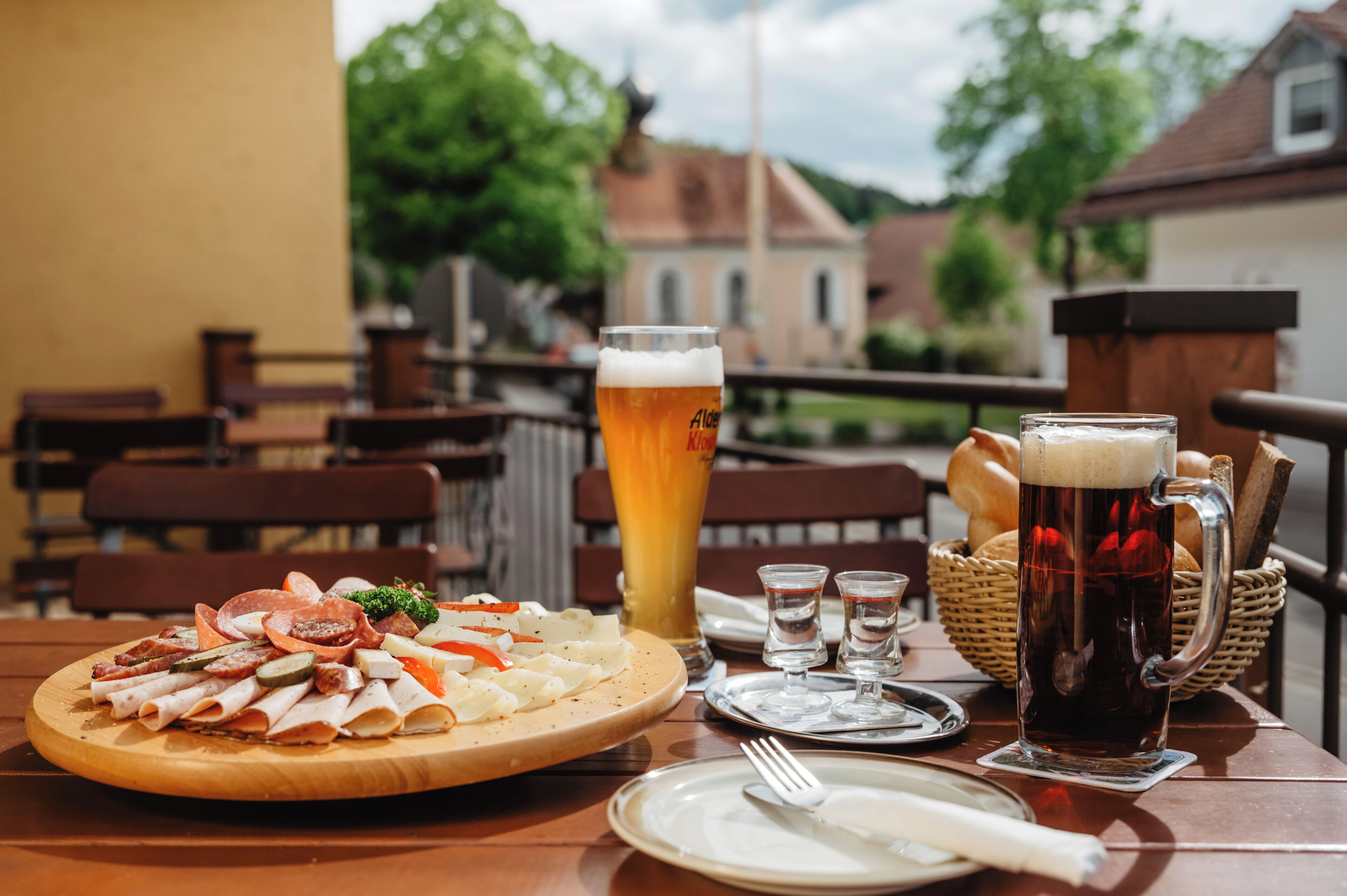 Uma mesa com um prato de carnes fatiadas, um copo alto de cerveja e uma caneca de chopp.