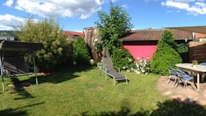 Um quintal com mesa e cadeiras no terraço, balanço e um prédio vermelho ao fundo.