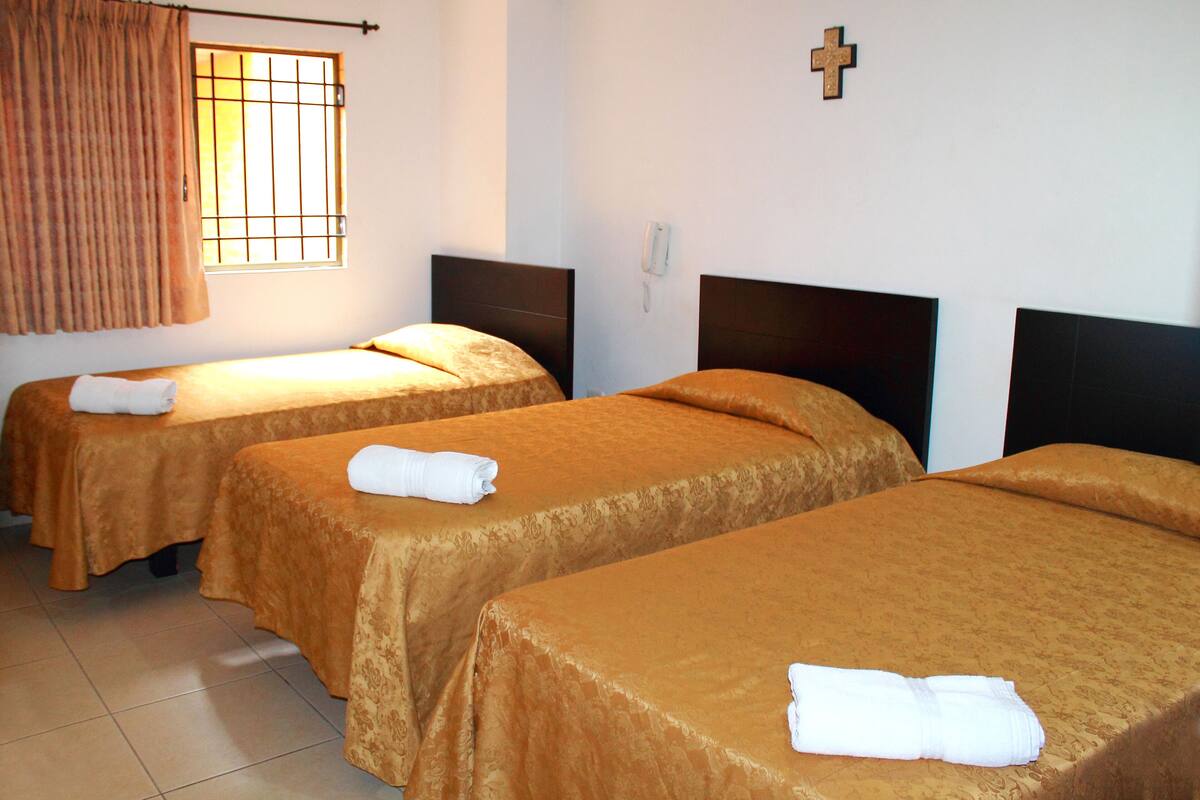 Quarto de hotel com duas camas individuais, cada uma com uma toalha branca dobrada.