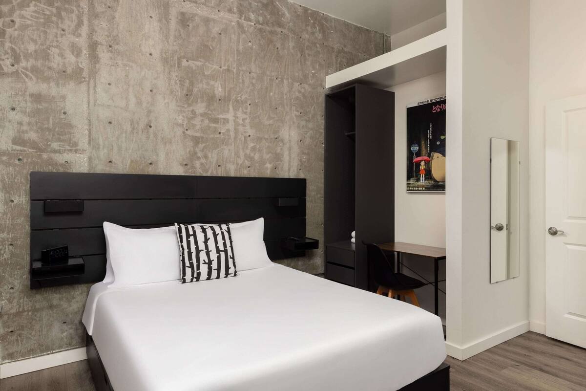 Quarto moderno com cama grande, parede de concreto, escrivaninha e espelho.