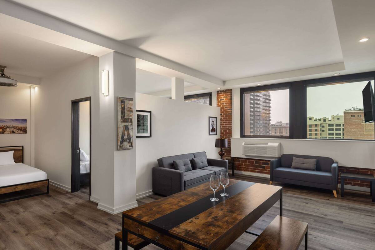 Um apartamento moderno com área de jantar, dois sofás, uma cama e uma janela grande com vista para a cidade.