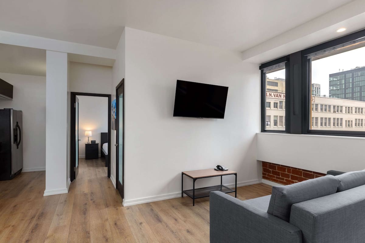 Uma sala de estar moderna com uma TV de tela plana na parede, um sofá cinza e uma pequena mesa de madeira.