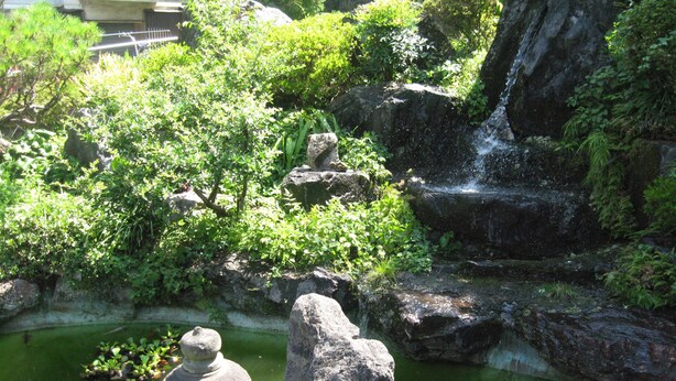 Um jardim tranquilo com um pequeno lago, um lampião de pedra e uma cascata.