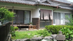 Uma casa japonesa tradicional com telhado de telhas, um pequeno jardim com lago e uma mesa e cadeiras de madeira ao ar livre.