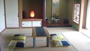 Um quarto japonês tradicional com tatames, uma mesa baixa, almofadas e portas deslizantes.