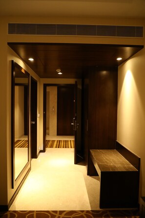 Um corredor de hotel com chão coberto por carpete, um banco e um espelho à esquerda.