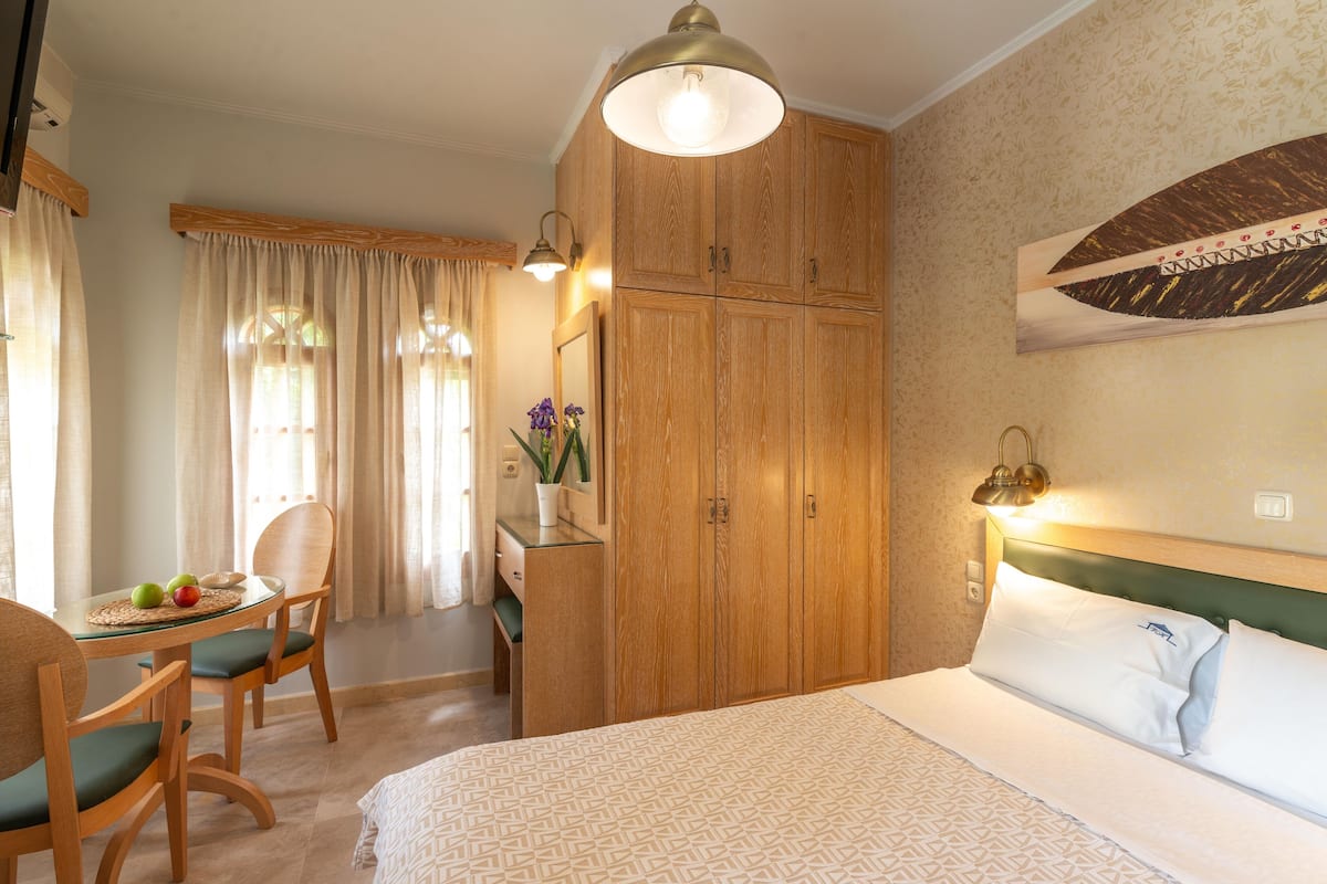 Quarto de hotel com cama, escrivaninha e cadeira, guarda-roupa e mesa de jantar com cadeiras.