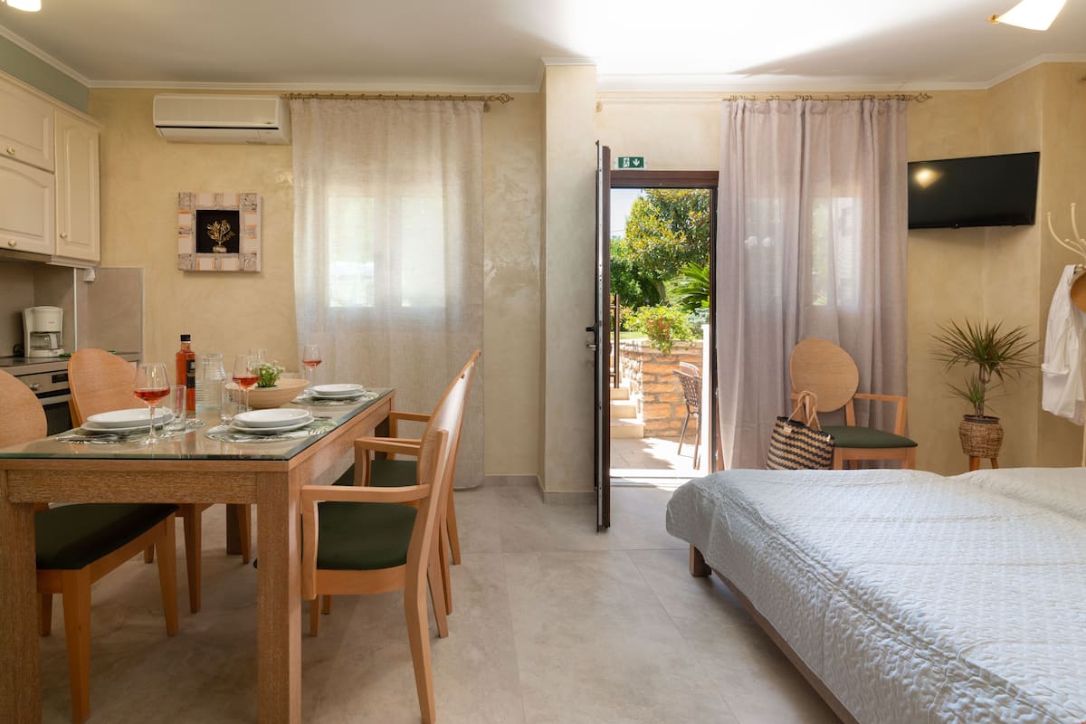 Quarto com mesa de jantar posta para dois, cama, televisão fixada na parede e porta que dá para uma área externa.