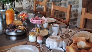 Uma mesa de café da manhã com diversos alimentos, um vaso de flores e uma parede de pedra ao fundo.