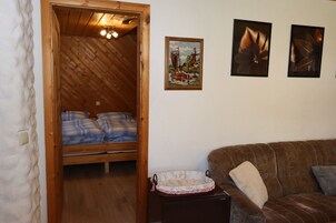 Quarto aconchegante com teto de madeira, cama com roupa de cama azul e branca, sofá marrom e duas obras de arte emolduradas na parede.