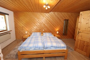 Quarto com painéis de madeira, uma cama, duas mesas de cabeceira e uma janela.